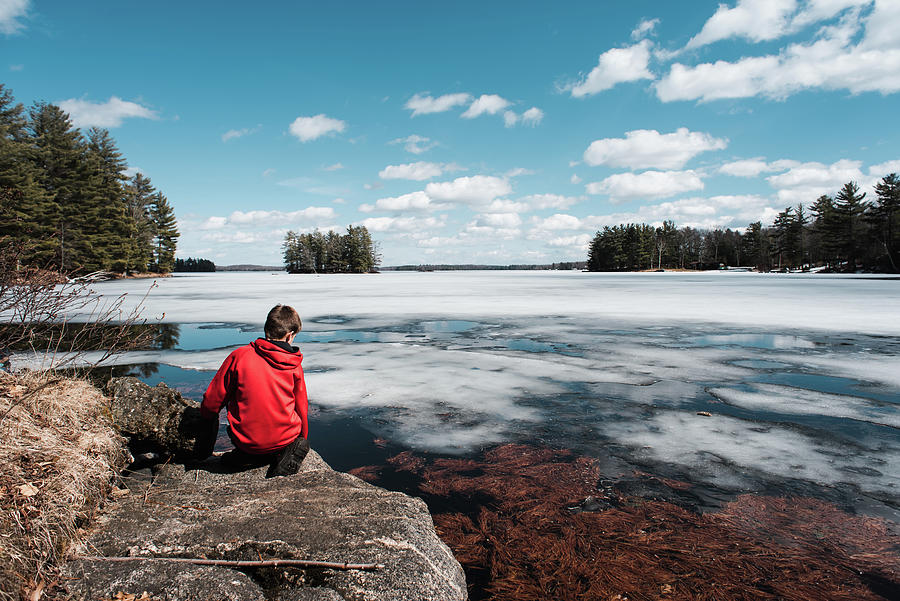 Boy Sitting On The Rocky Shore Of An Icy Lake During Spring Thaw ...