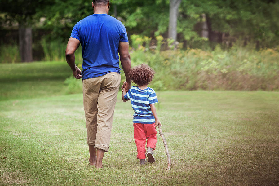 Father And Son Holding Hands While Walking On Grassy Field Photograph