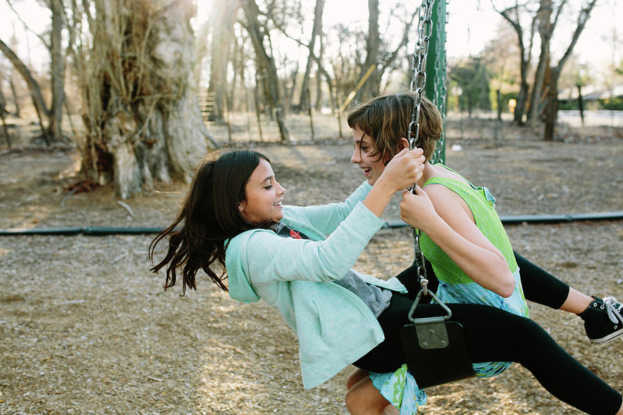 Happy Sisters Swinging Against Bare Trees In Playground Photograph By