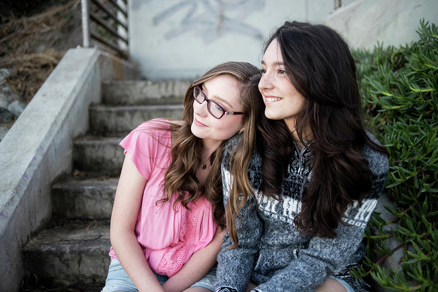 Smiling Sisters Looking Away While Sitting On Steps At Beach Photograph ...