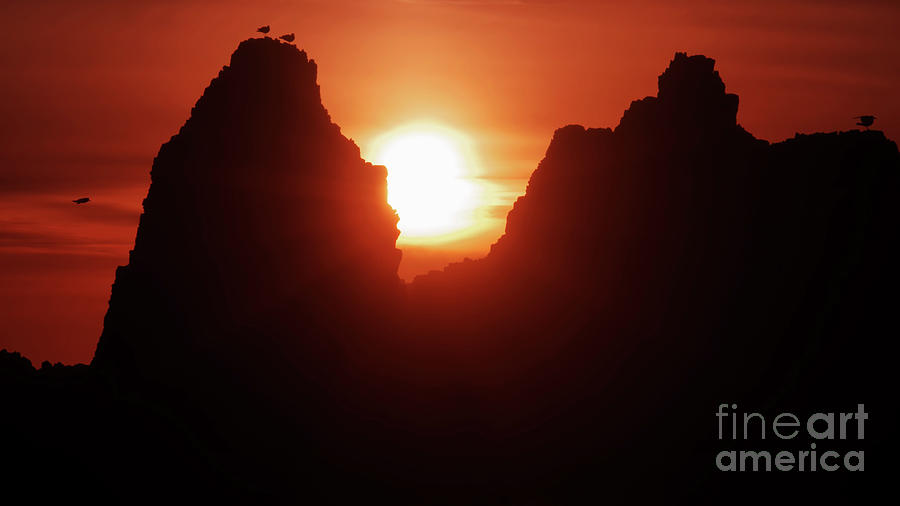 Sunfall between rocks on the ocean Photograph by Jeff Swan