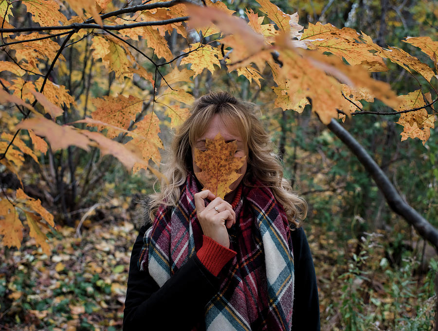 Woman Holding Maple Leaf On Face While Standing Amidst Trees In Forest