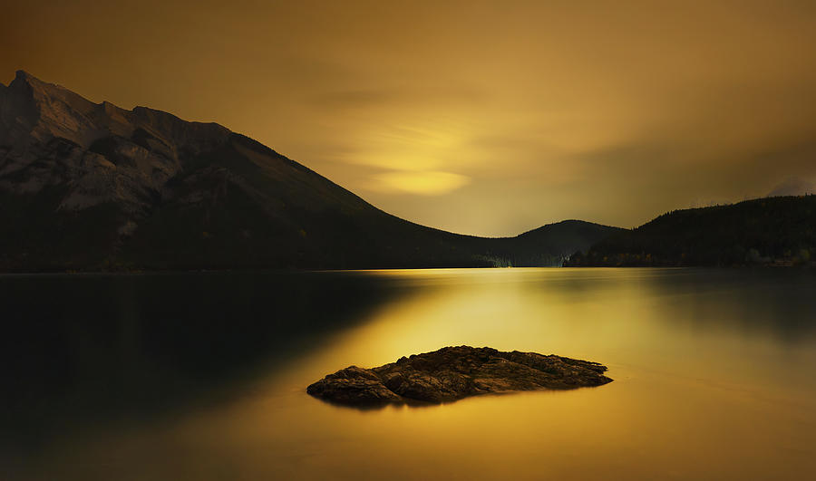 Night long exposure of a mountain lake glowing from the moon that is ...